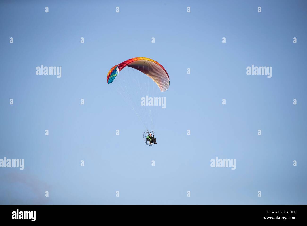A solo flier enjoying a paramotor flight with multicoloured canopy on a ...