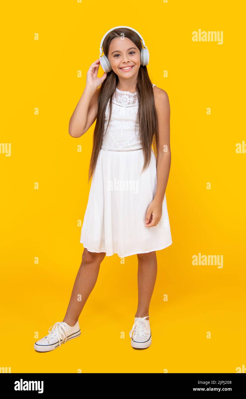 positive teen girl listen music in headphones on yellow background ...