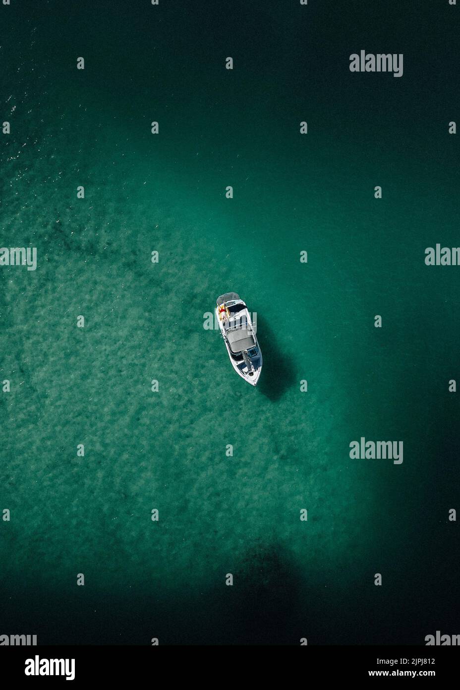 A vertical top view of a lonely boat floating in a blue waters of the ...