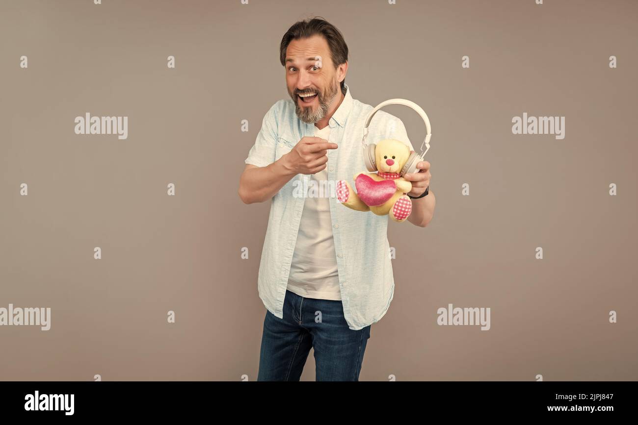 Love is the music. Happy senior man point at teddy bear. Music will ...