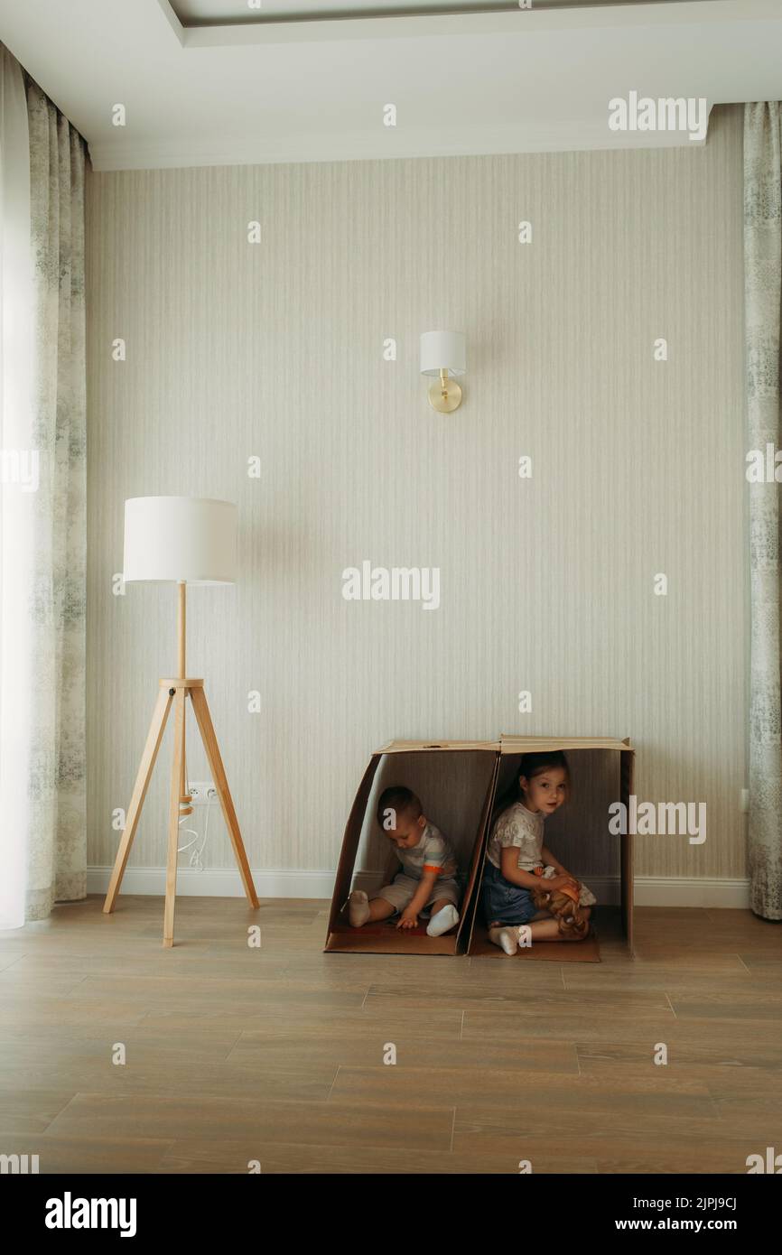 Children sit in a cardboard house made of cardboard boxes. Kids are ...