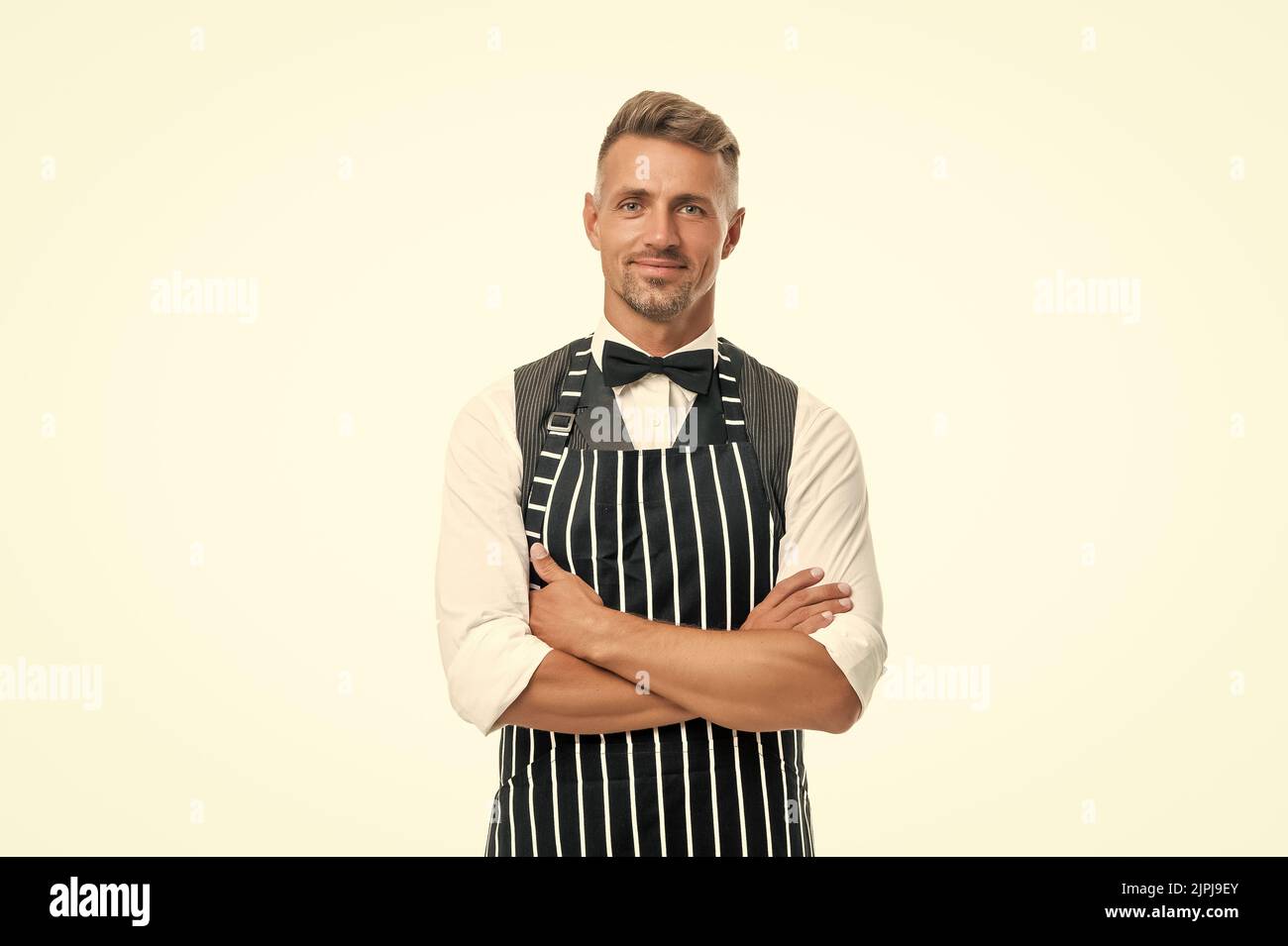 Happy chef in cook apron and bow keeping arms crossed isolated on white ...