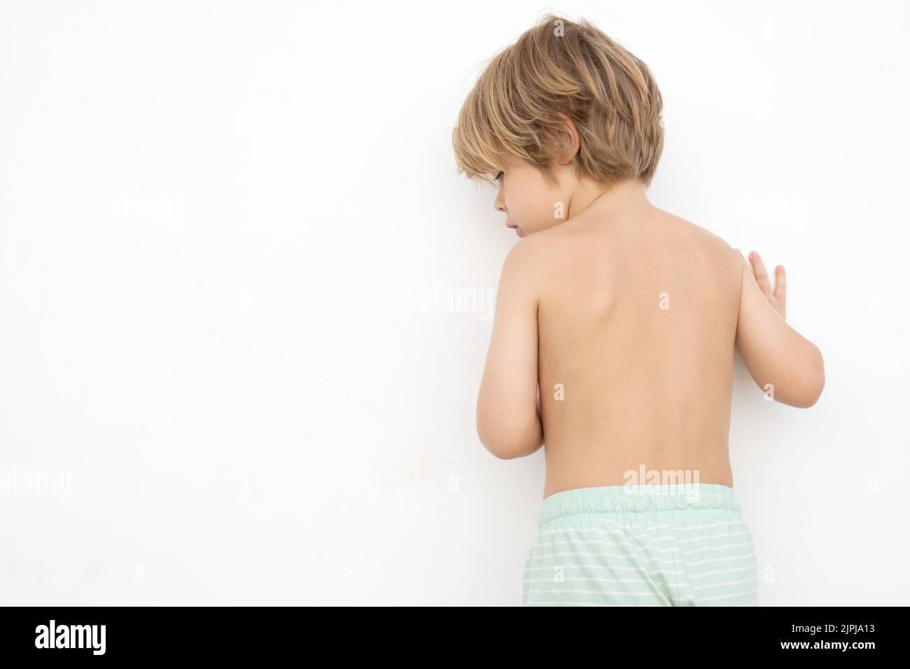 Back view of child boy standing against white wall in a summer day ...