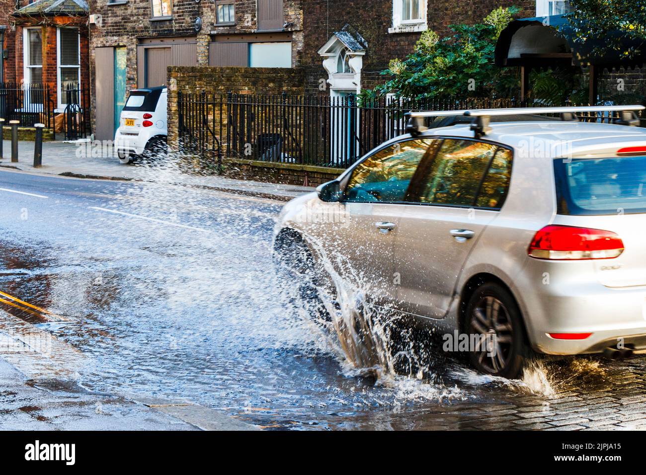 A car drives through a large roadside puddle caused by a mains water ...