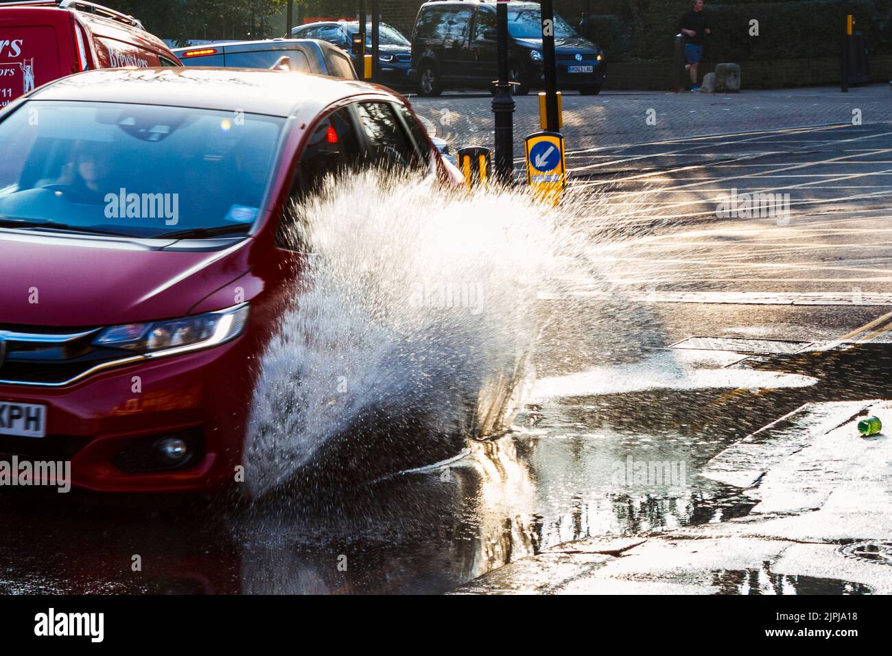 A car drives through a large roadside puddle caused by a mains water ...