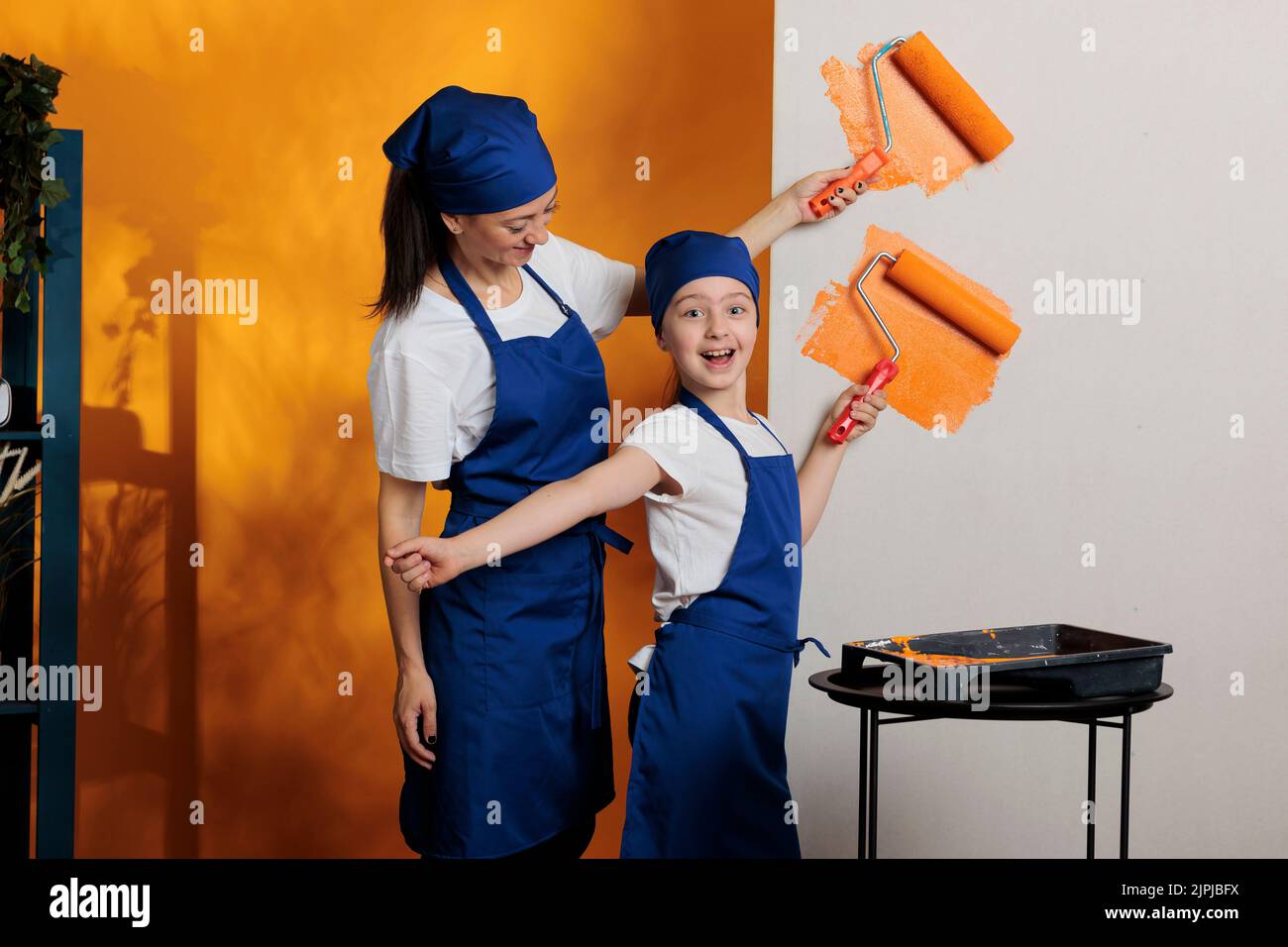 Happy people painting orange walls to redecorate house room, using ...