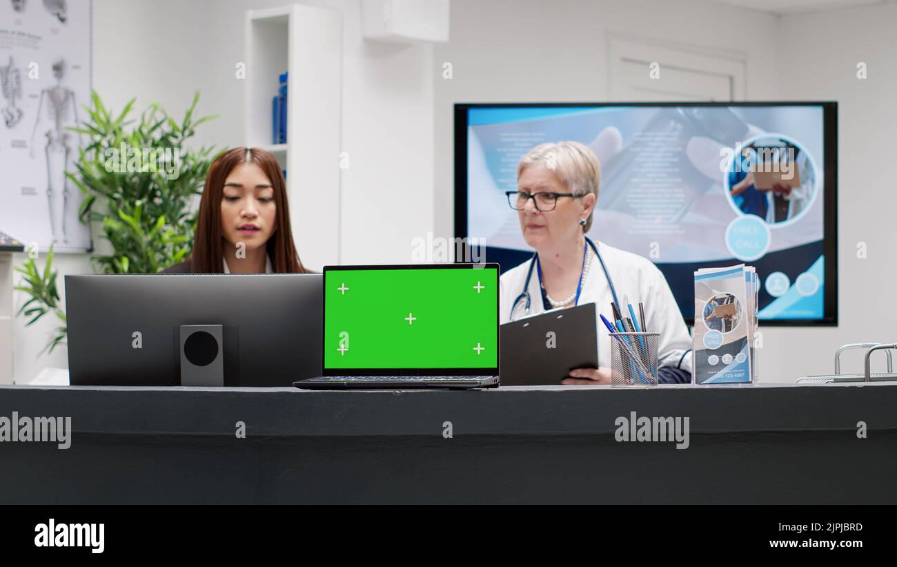 Medical staff working at reception desk with greenscreen display on ...