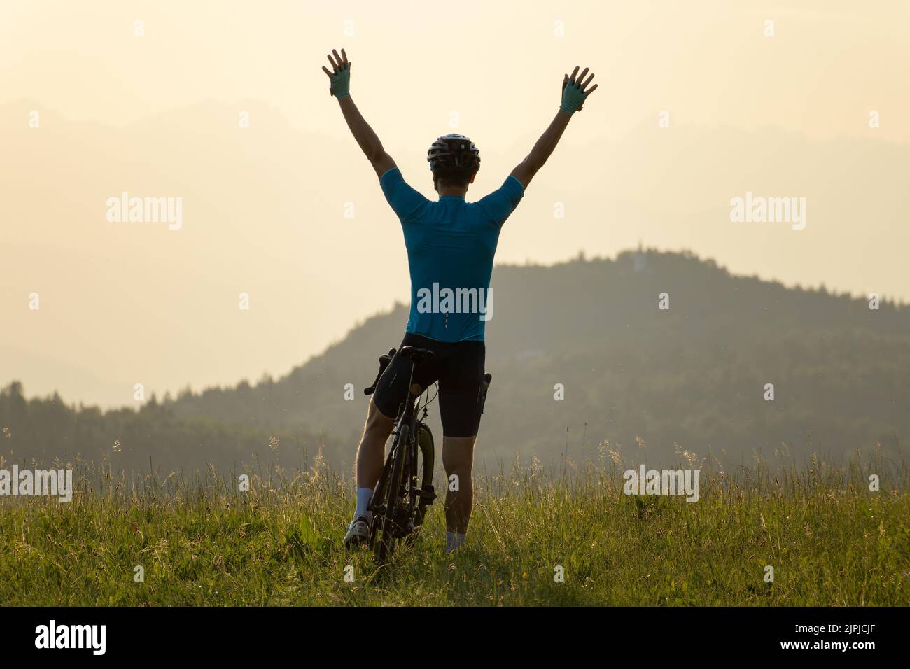 Male athlete professional racing cyclist riding a bike with arms raised ...