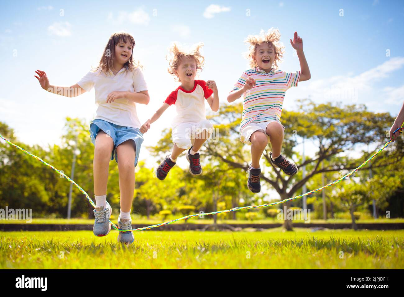 Happy kids play outdoor. Children skipping rope in sunny garden. Summer ...