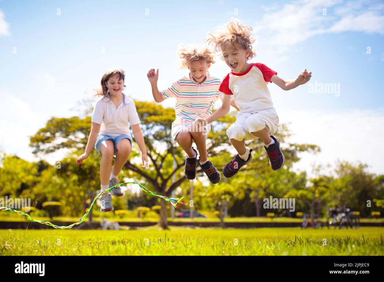 Happy kids play outdoor. Children skipping rope in sunny garden. Summer ...