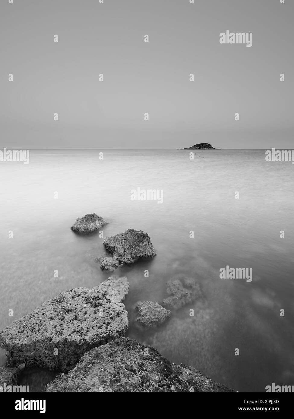 A vertical grayscale of the sea with rocks on the coast Stock Photo - Alamy