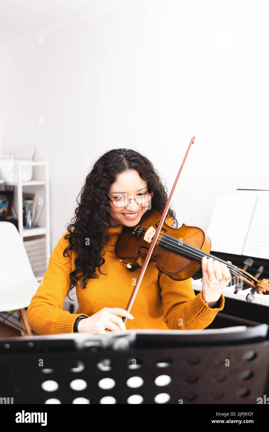 Smiling brunette woman wearing a yellow sweater, and playing violin by ...