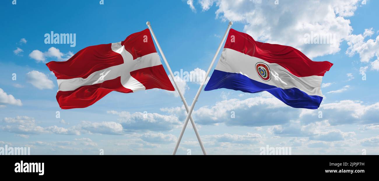 two crossed flags Paraguay and Denmark waving in wind at cloudy sky ...