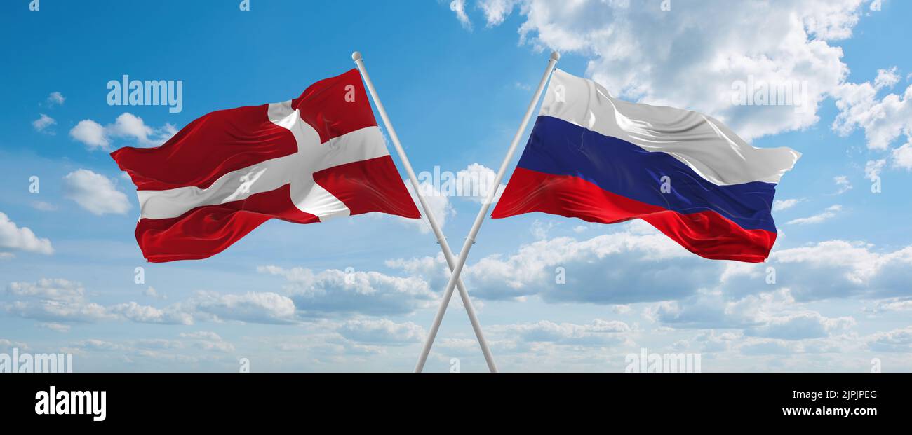 two crossed flags Russia and Denmark waving in wind at cloudy sky ...