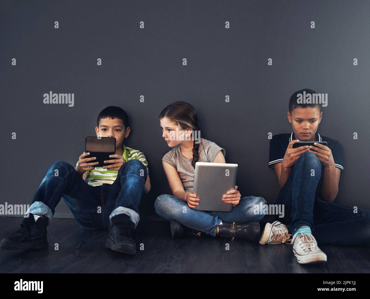Tweens and their screens. Studio shot of kids sitting on the floor and ...