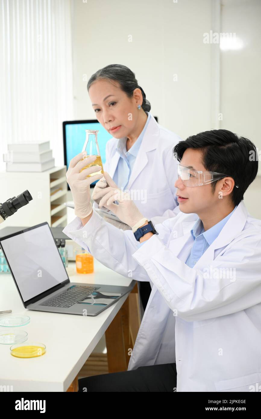 A talented young Asian male scientist is holding a beaker, doing a ...