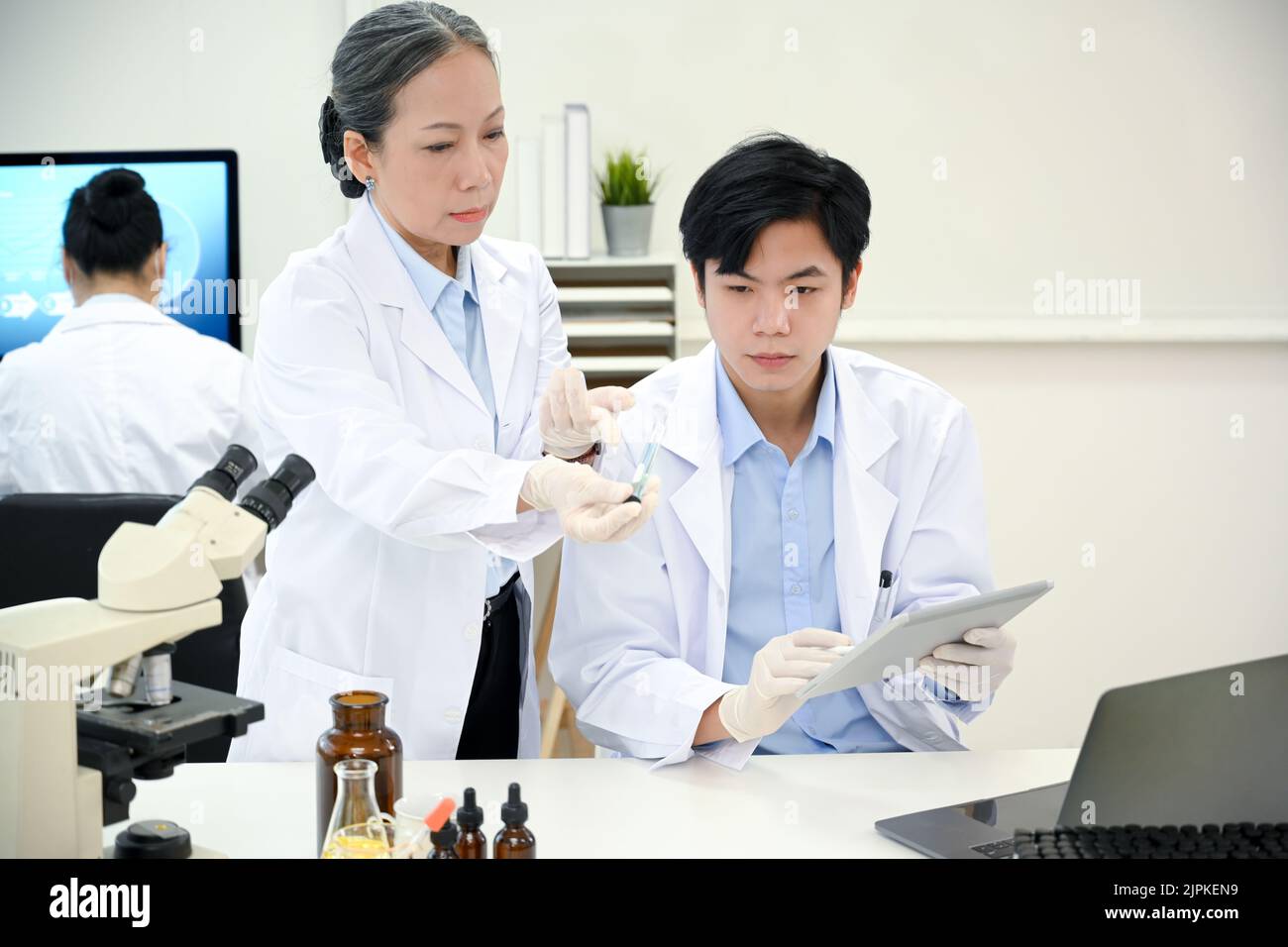 Two professional Asian scientists in white coat concentrating doing a chemical experiment ...