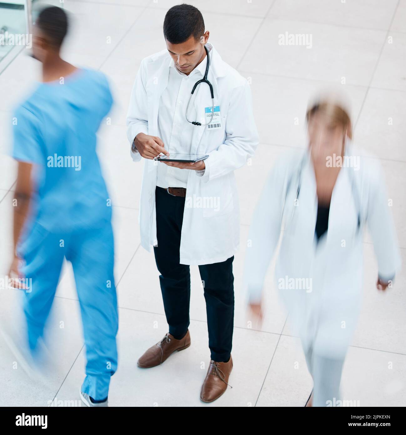 Busy hospital with doctor browsing on tablet for test results, patient ...