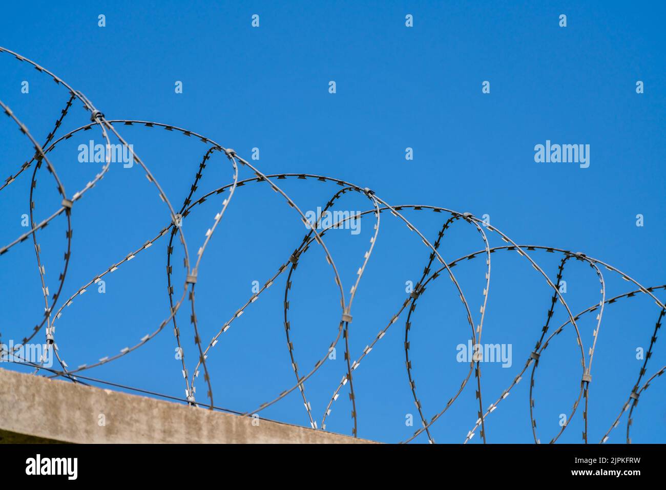 A low angle shot of barbed wires on a prison wall against a blue sky ...