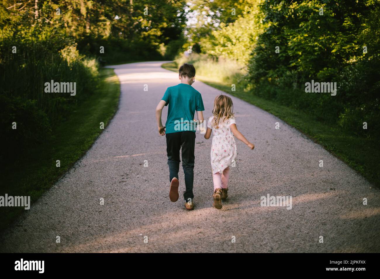 Brother and sister run along path through green forest Stock Photo - Alamy