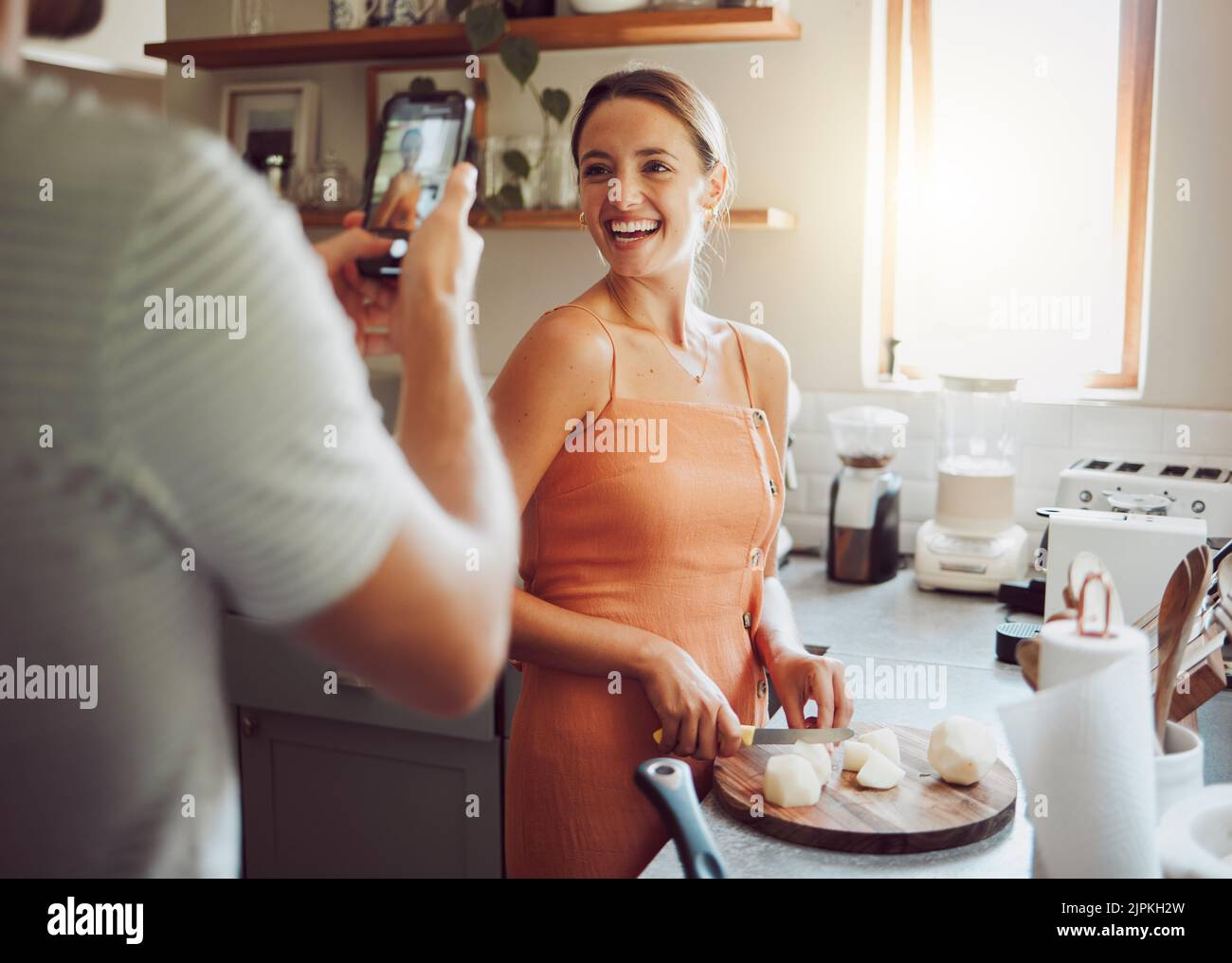 Woman cooking with husband taking a picture in kitchen on his mobile ...