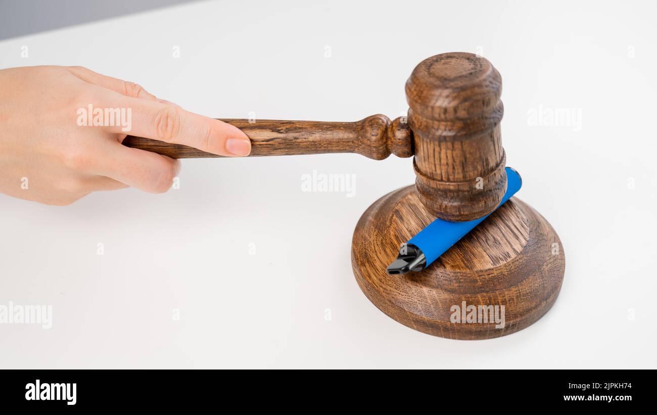 Judge hammering disposable vape with referee's gavel on white table ...
