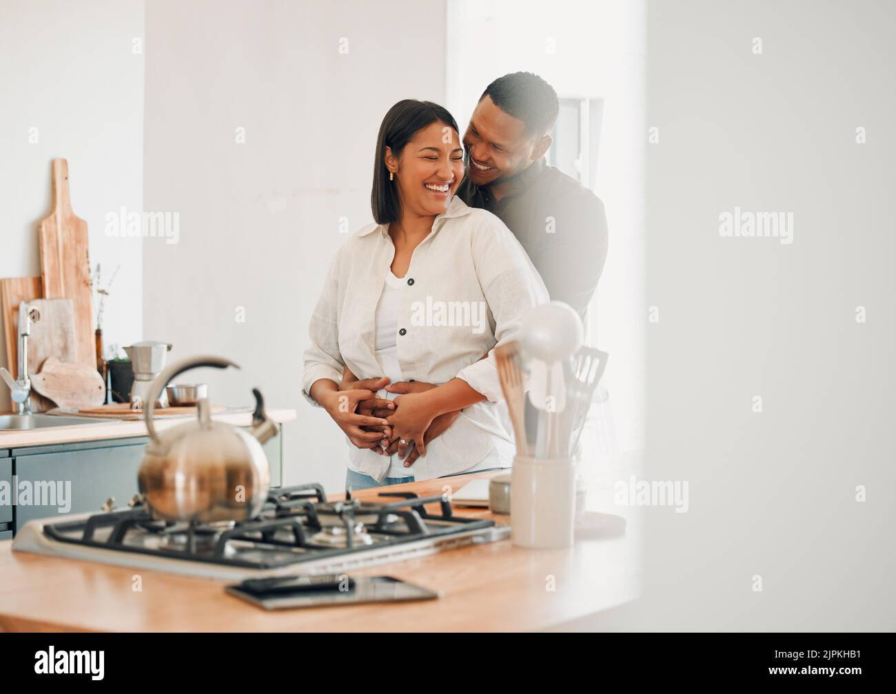 Loving, happy and hugging couple relaxing in the kitchen at home ...