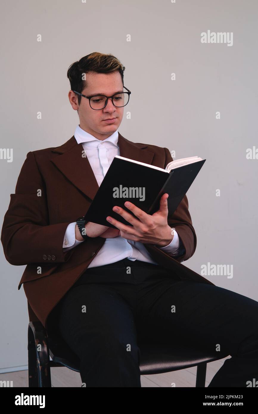 Studious elegant man sitting in front of a white wall while reading a ...