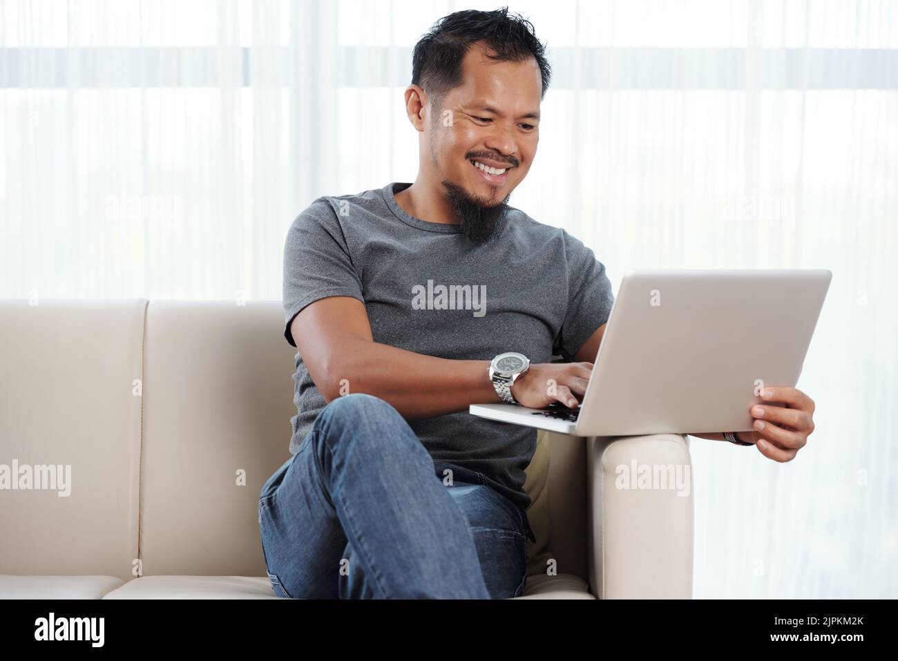 Portrait of happy Filipino man with laptop sitting on sofa Stock Photo ...