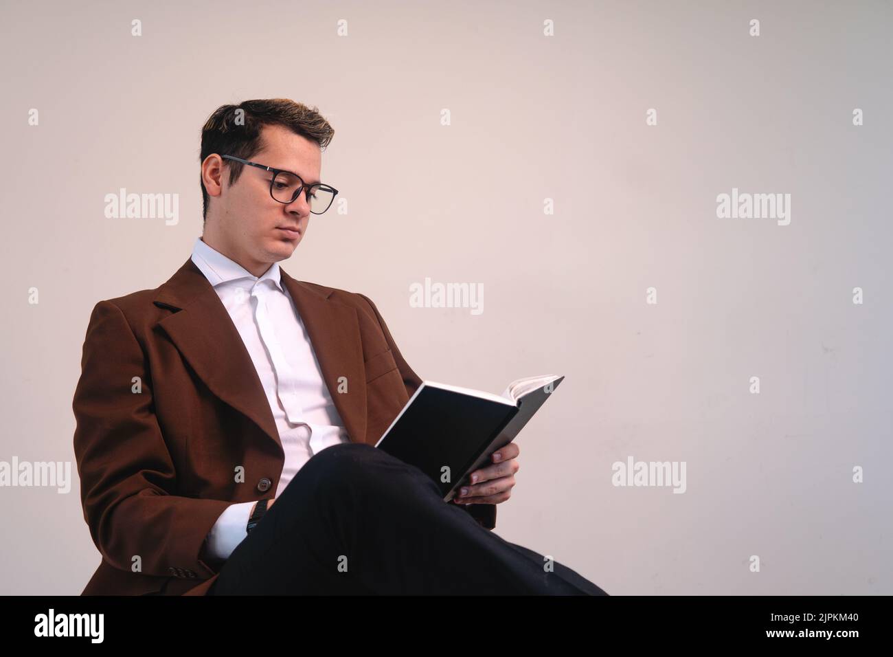 Intellectual man dressed in a suit and glasses reading book sitting on ...