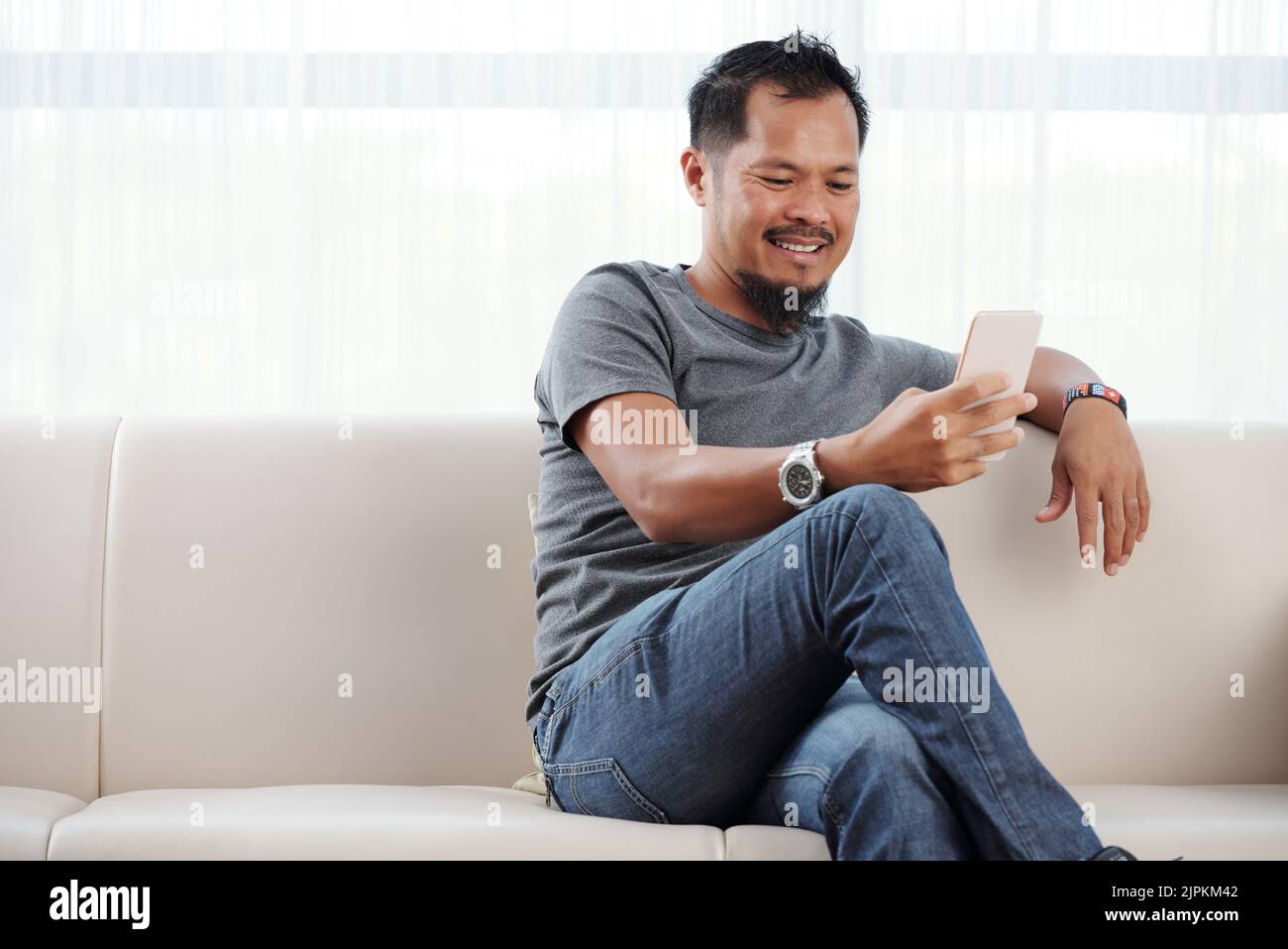 Filipino man sitting on sofa and reading messages in his phone Stock ...