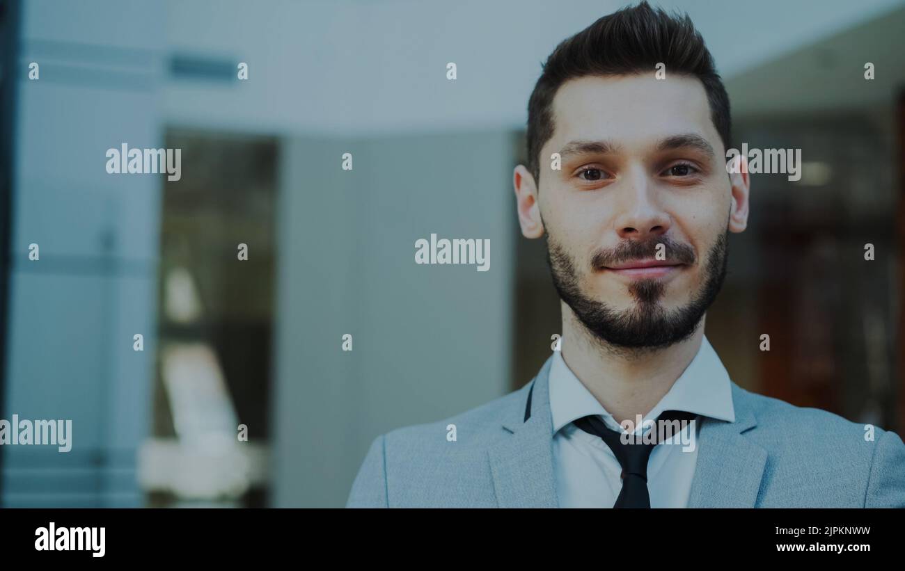 Portrait of successful young smiling businessman looking into camera in ...