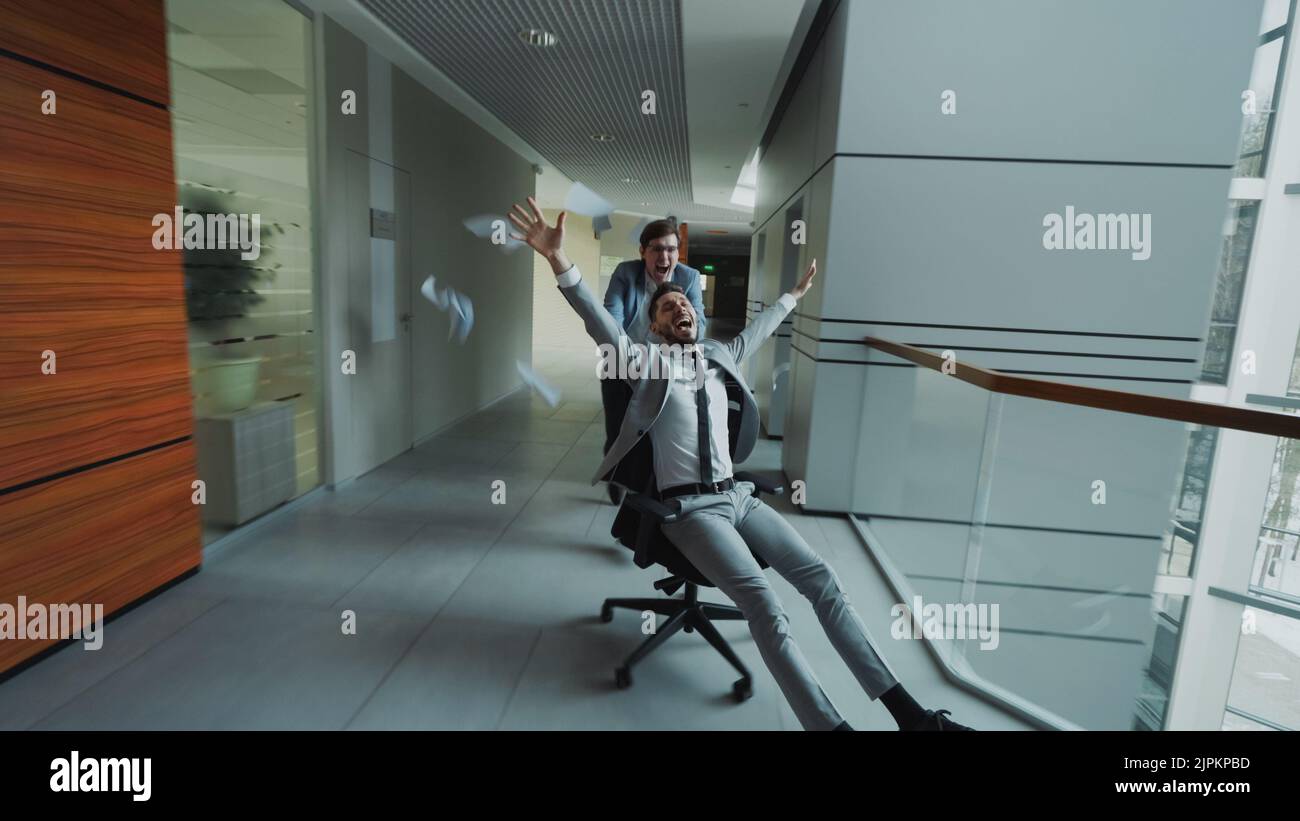 Two crazy businessmen riding office chair and throwing papers up while ...