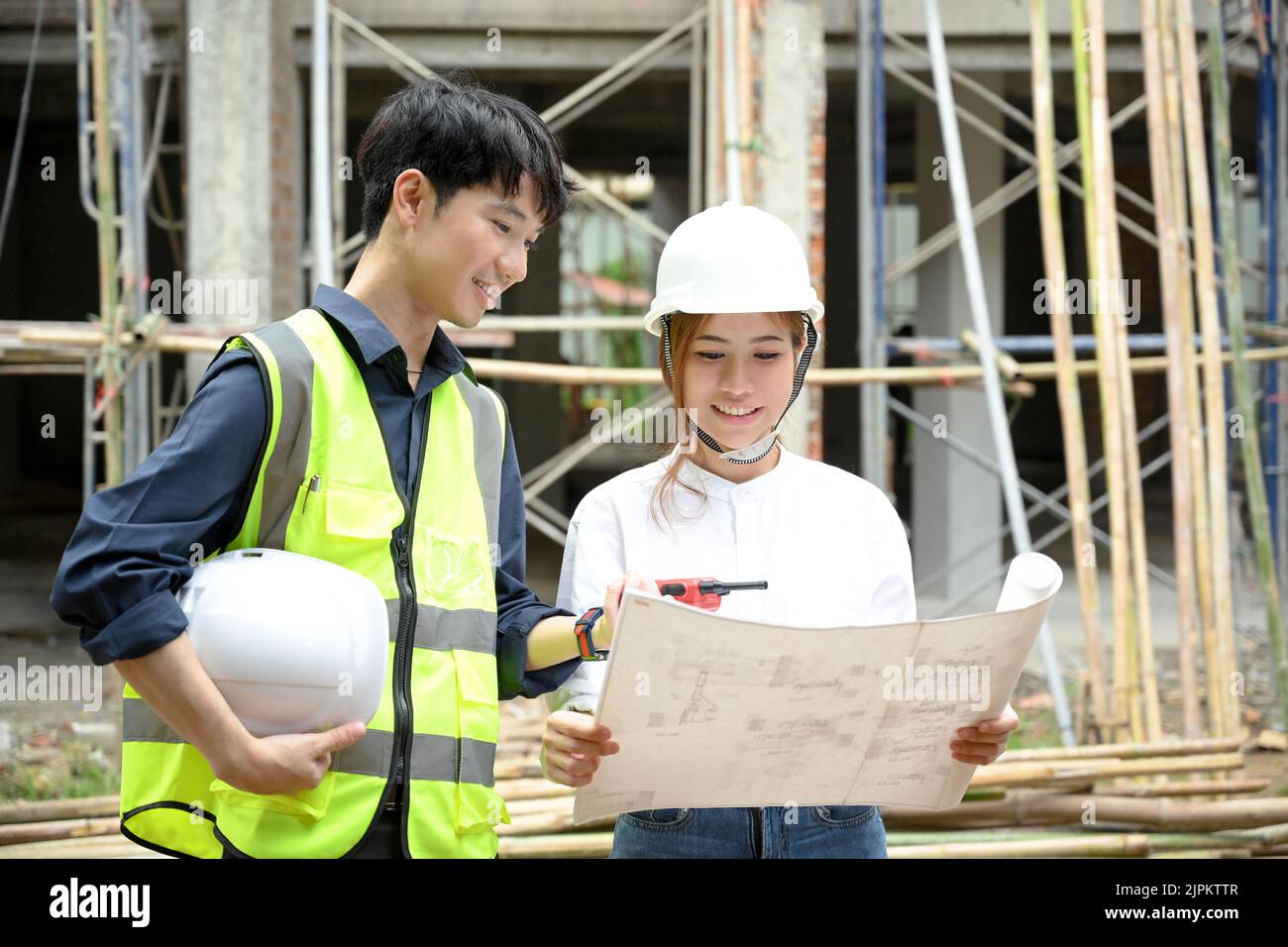 Attractive young Asian female architect looking at the blueprint while ...
