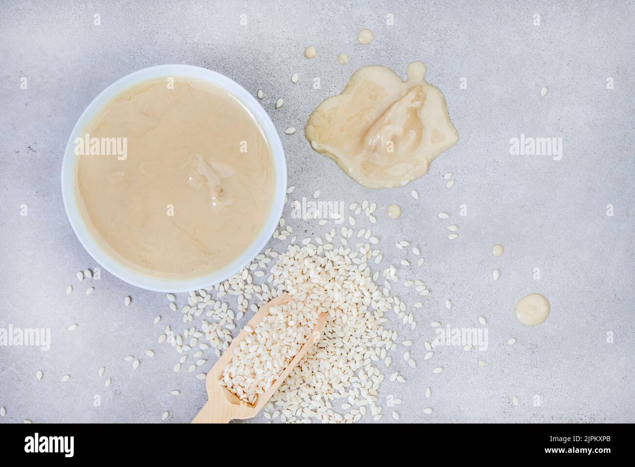 Pure sesame tahini with sesame seeds on mottled grey with copy space ...