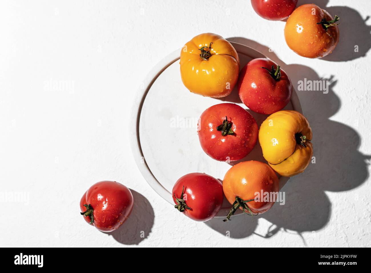 Fresh ripe colorful tomatoes on plate with hard shadows on white ...