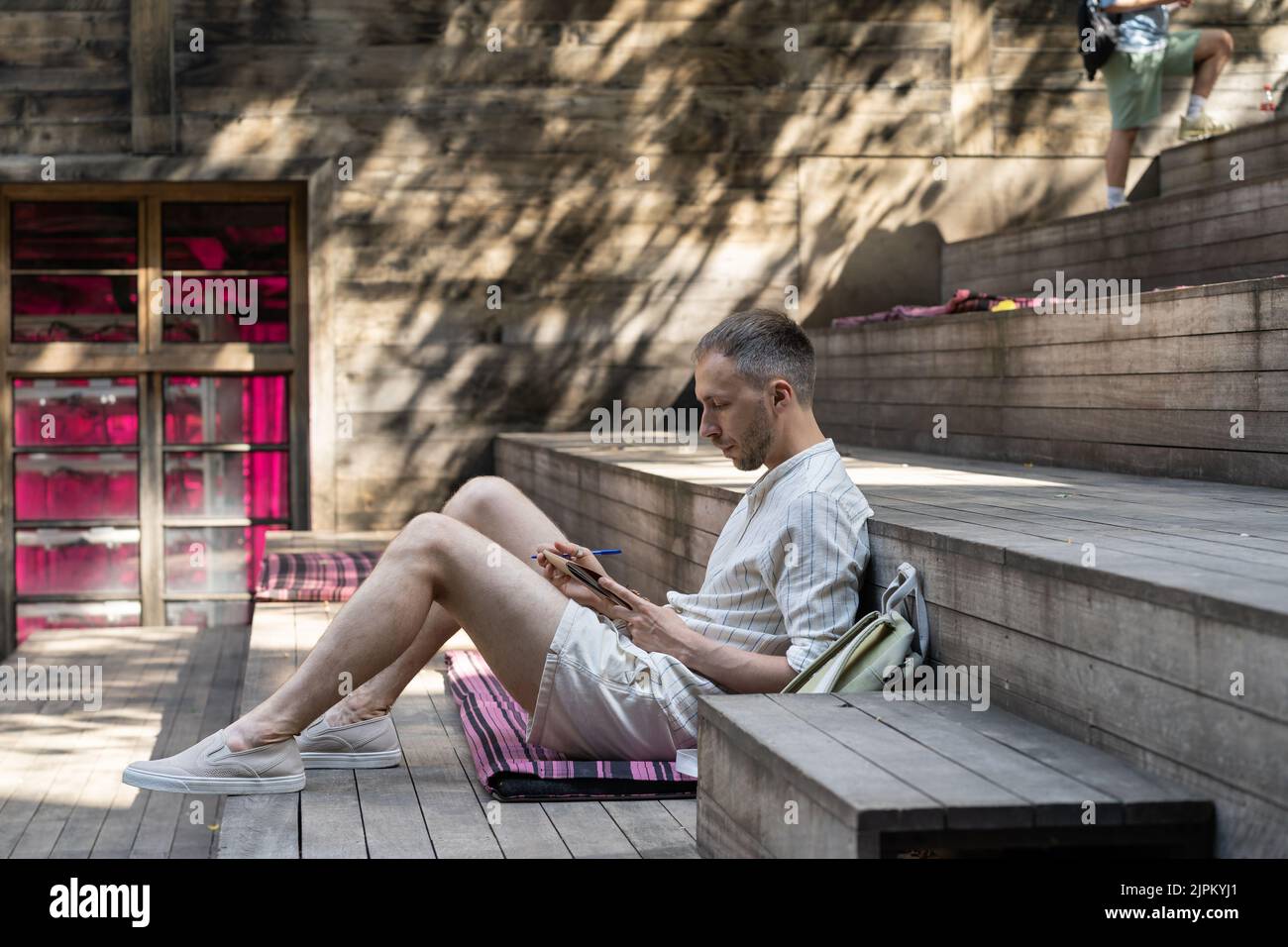 Stylish man drawer makes sketches in paper pad sitting on wooden step ...