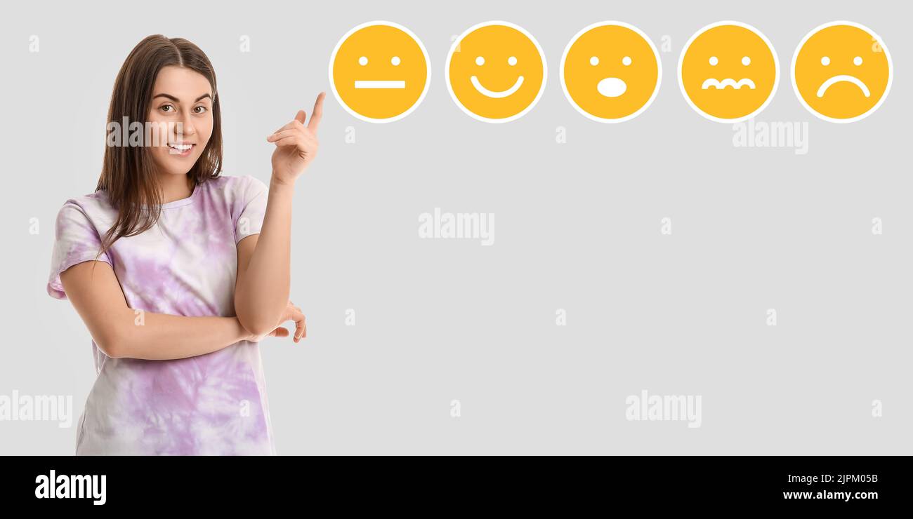 Pretty young woman pointing at many different emoticons on light ...
