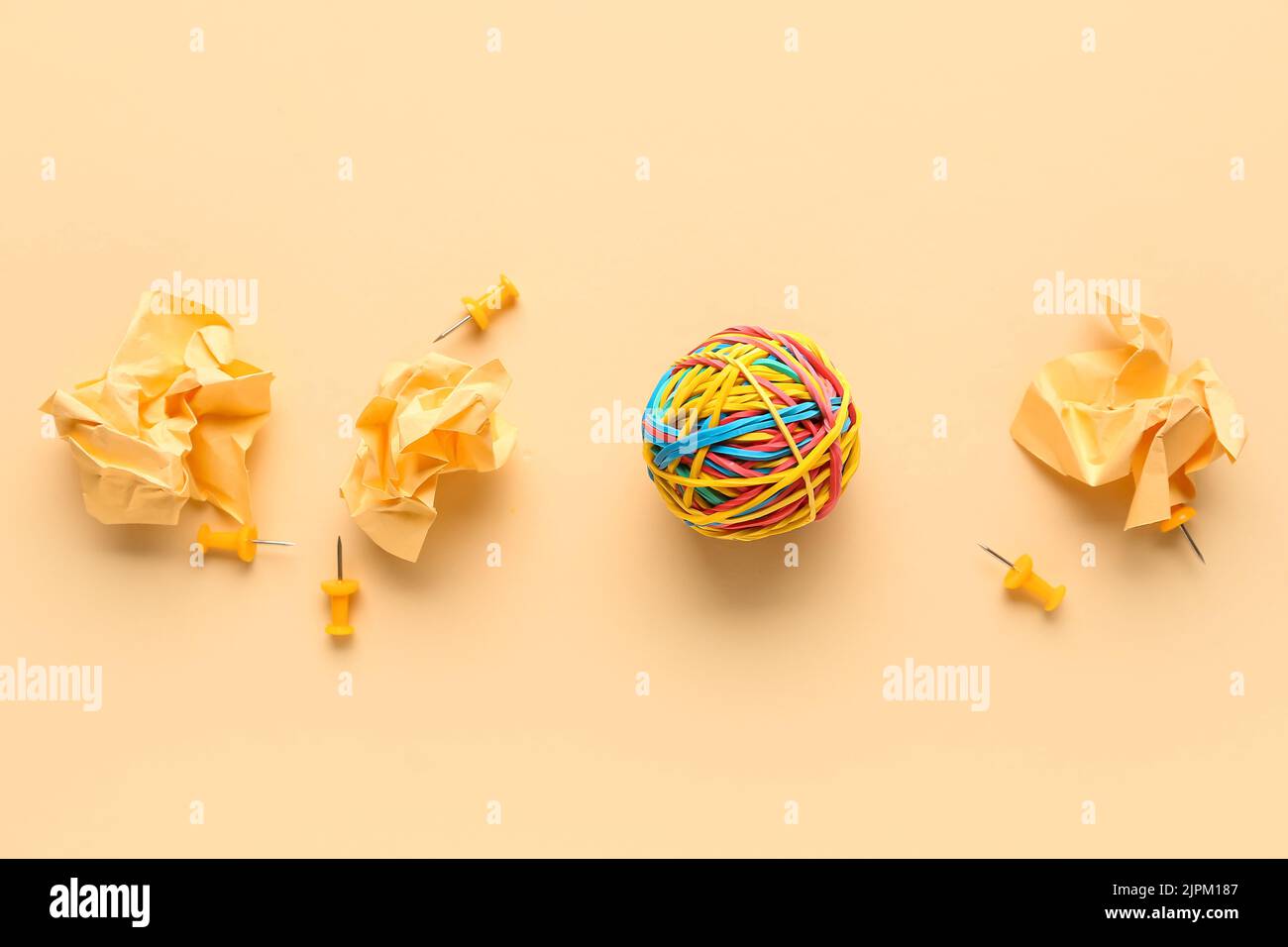 Colorful rubber band ball, crumpled paper and pins on beige background ...
