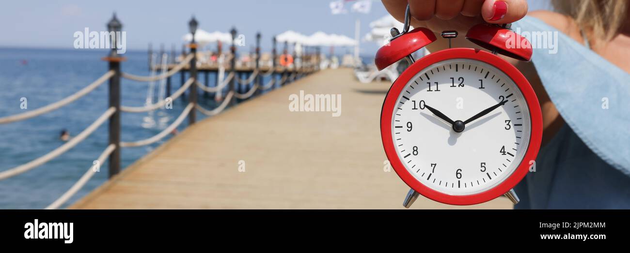 Alarm clock for ten in morning in female hand against backdrop of sea ...