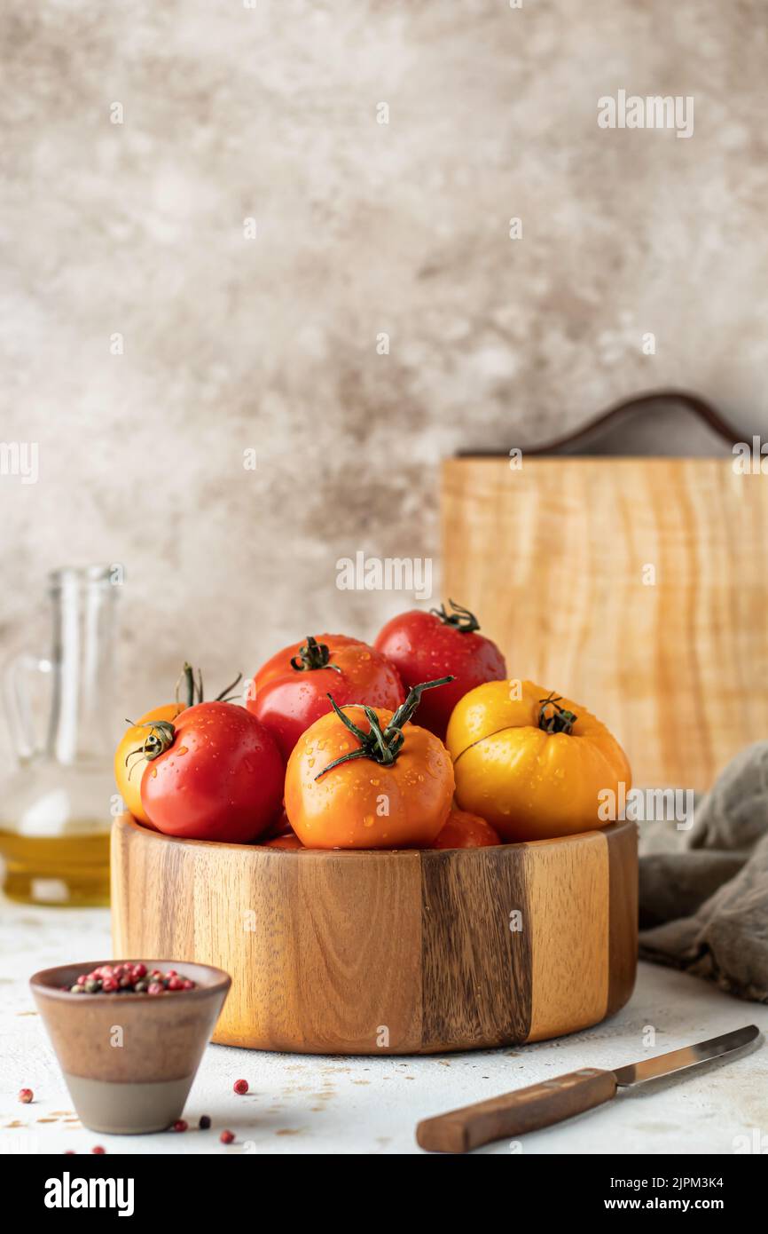 Wooden bowl of colorful tomatoes with knife, board, oil bottle and ...
