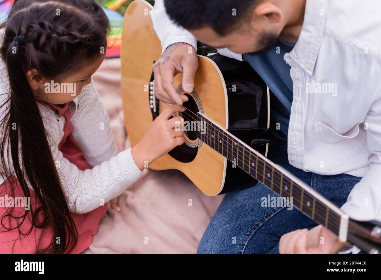 Preteen asian child playing acoustic guitar with father on blanket in ...