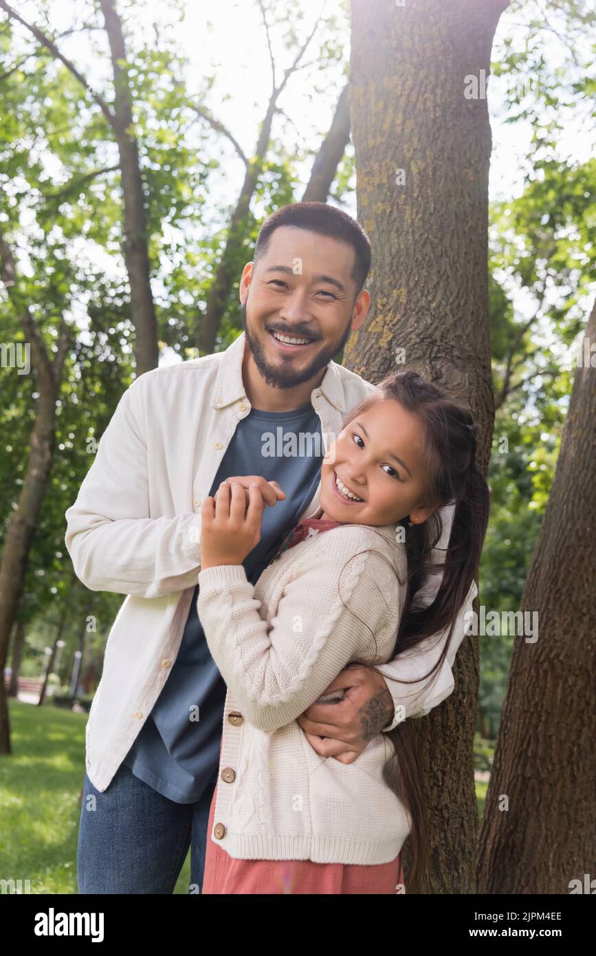 Positive asian father and daughter hugging and looking at camera in ...