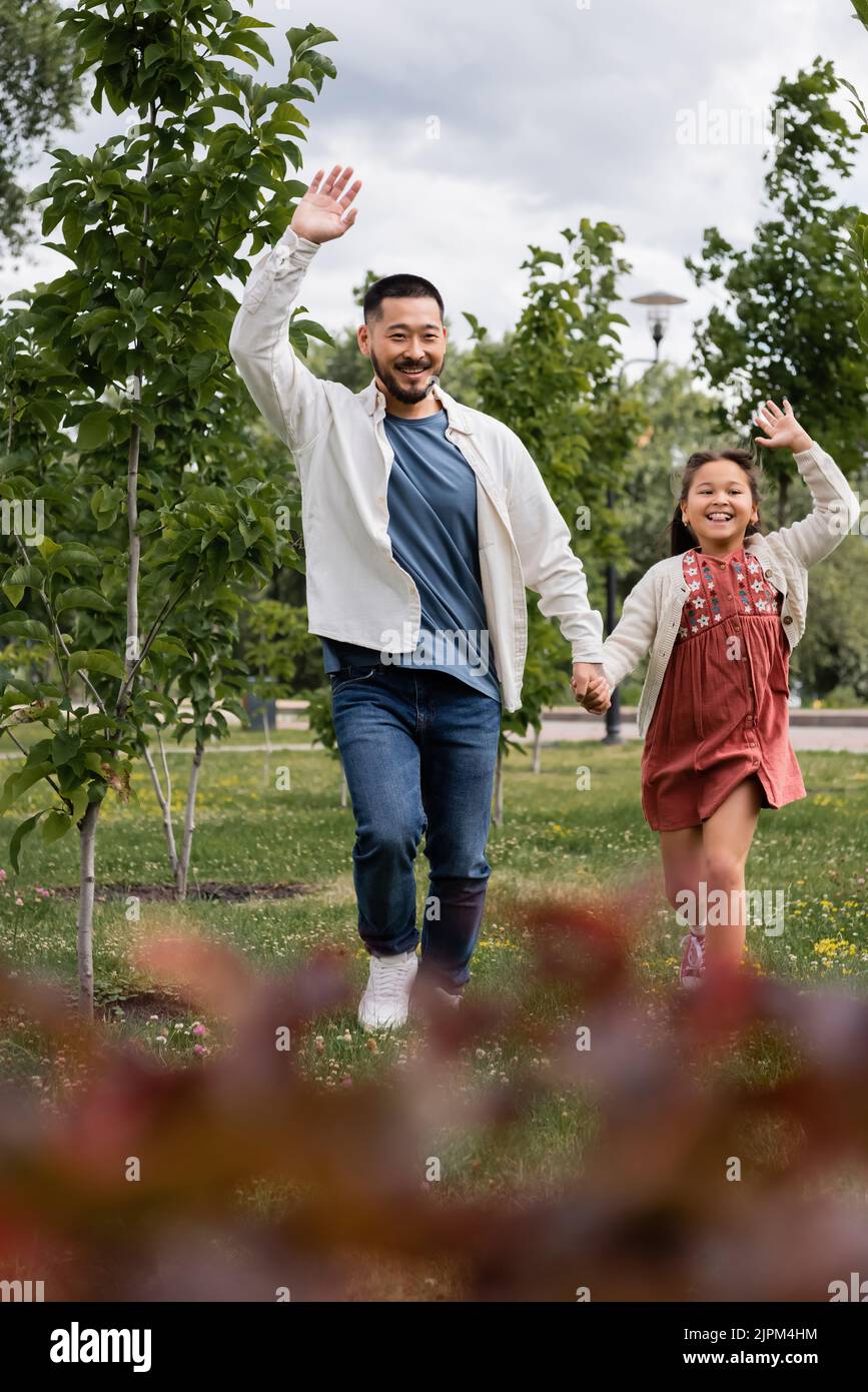 Happy asian father and child waving hands while running in park Stock ...