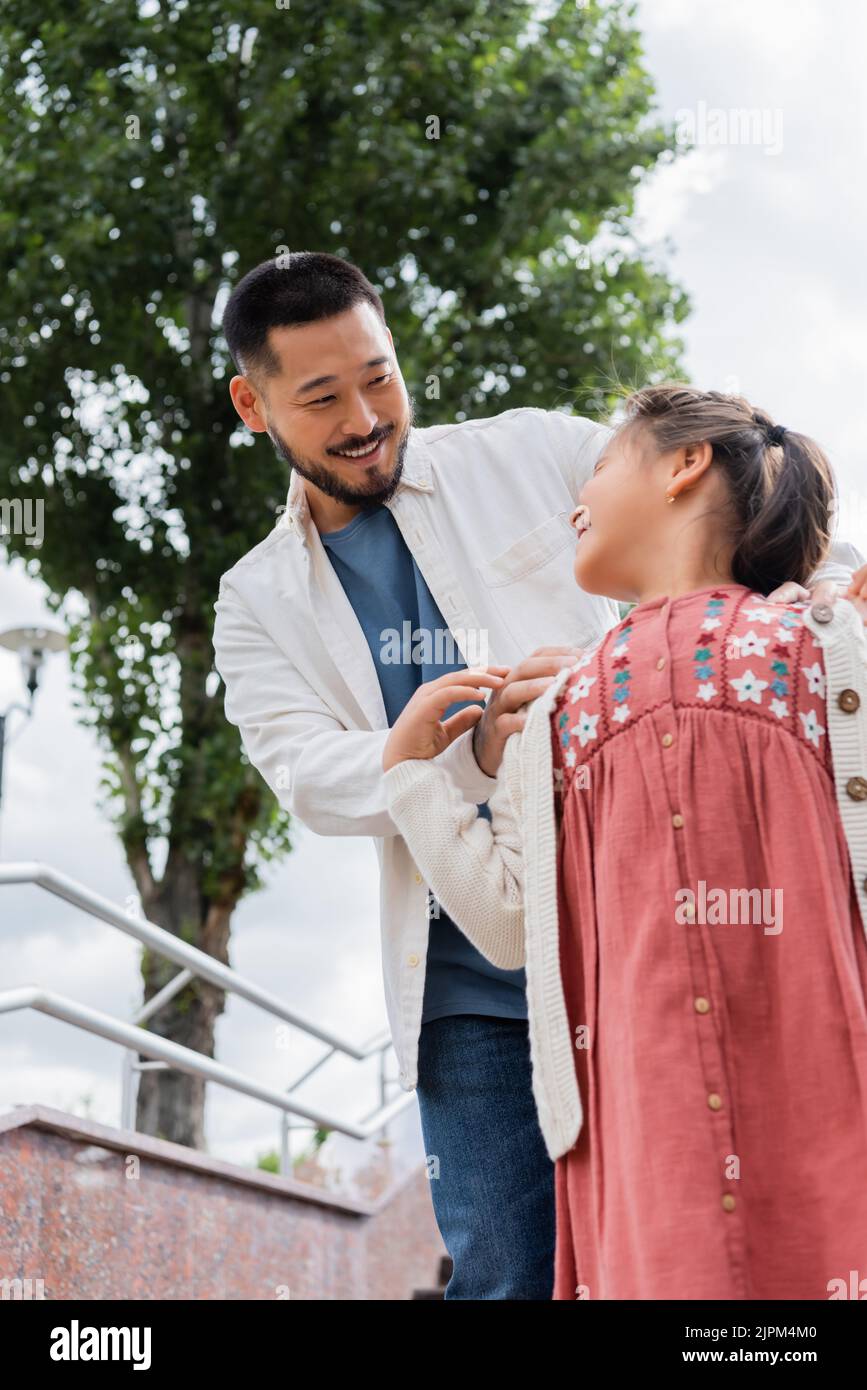 Low angle view of smiling asian dad looking at daughter in summer park ...