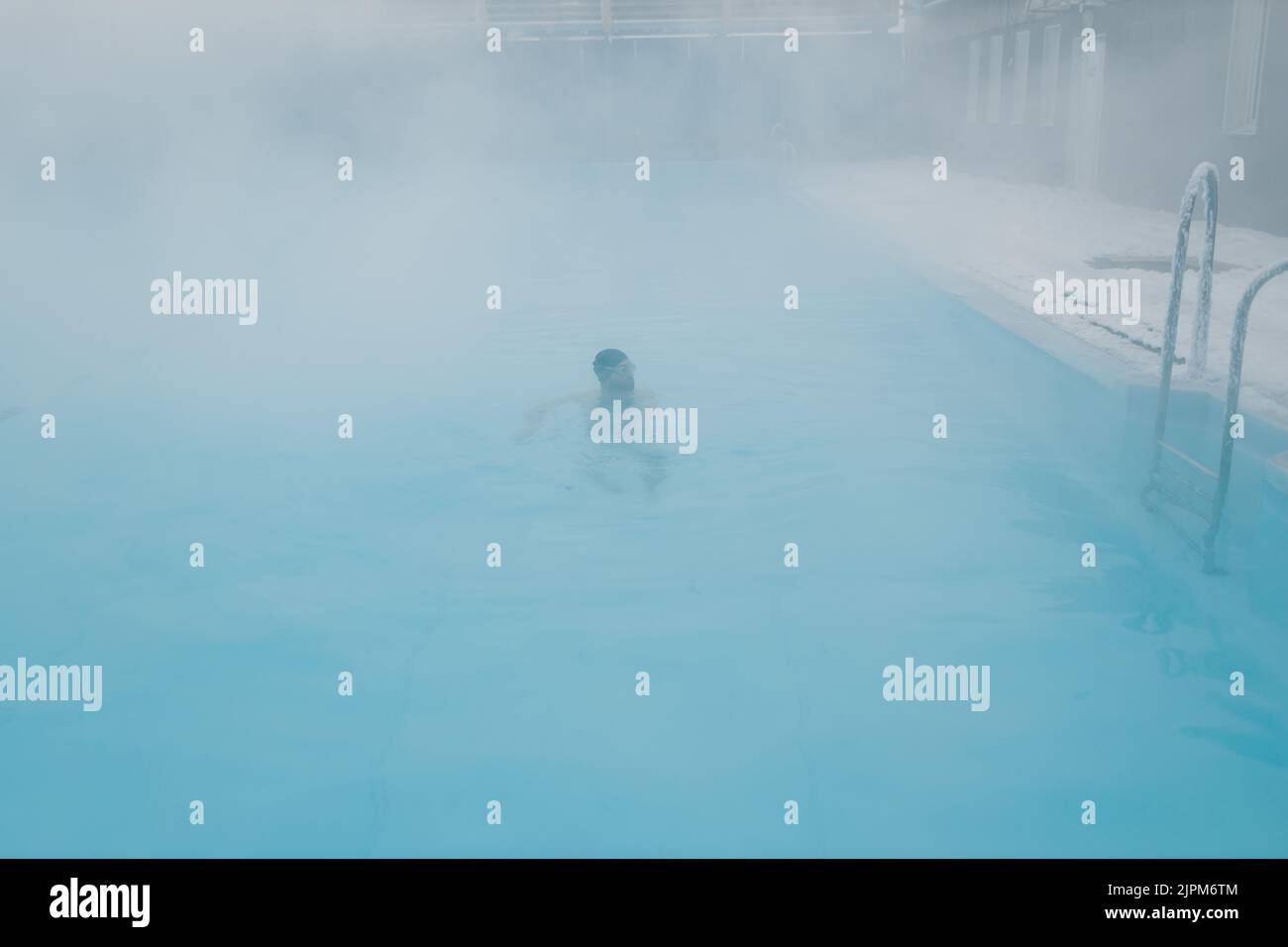 Fit swimmer male training swim in open winter swimming pool with fog ...