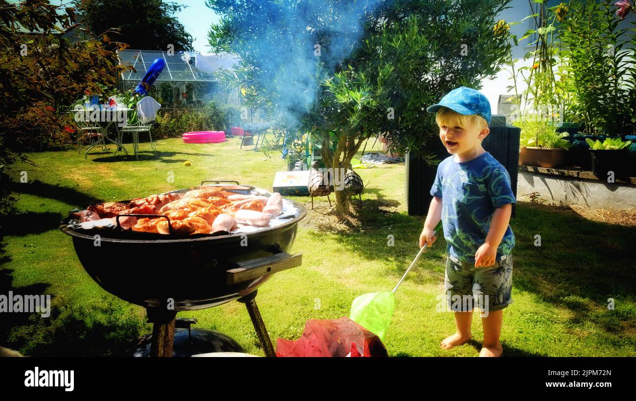 Young boy looking at smoking barbecue in a summer garden - John Gollop ...
