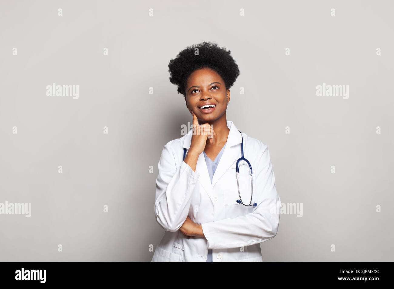 Attractive black woman doctor in white uniform looking up on white ...