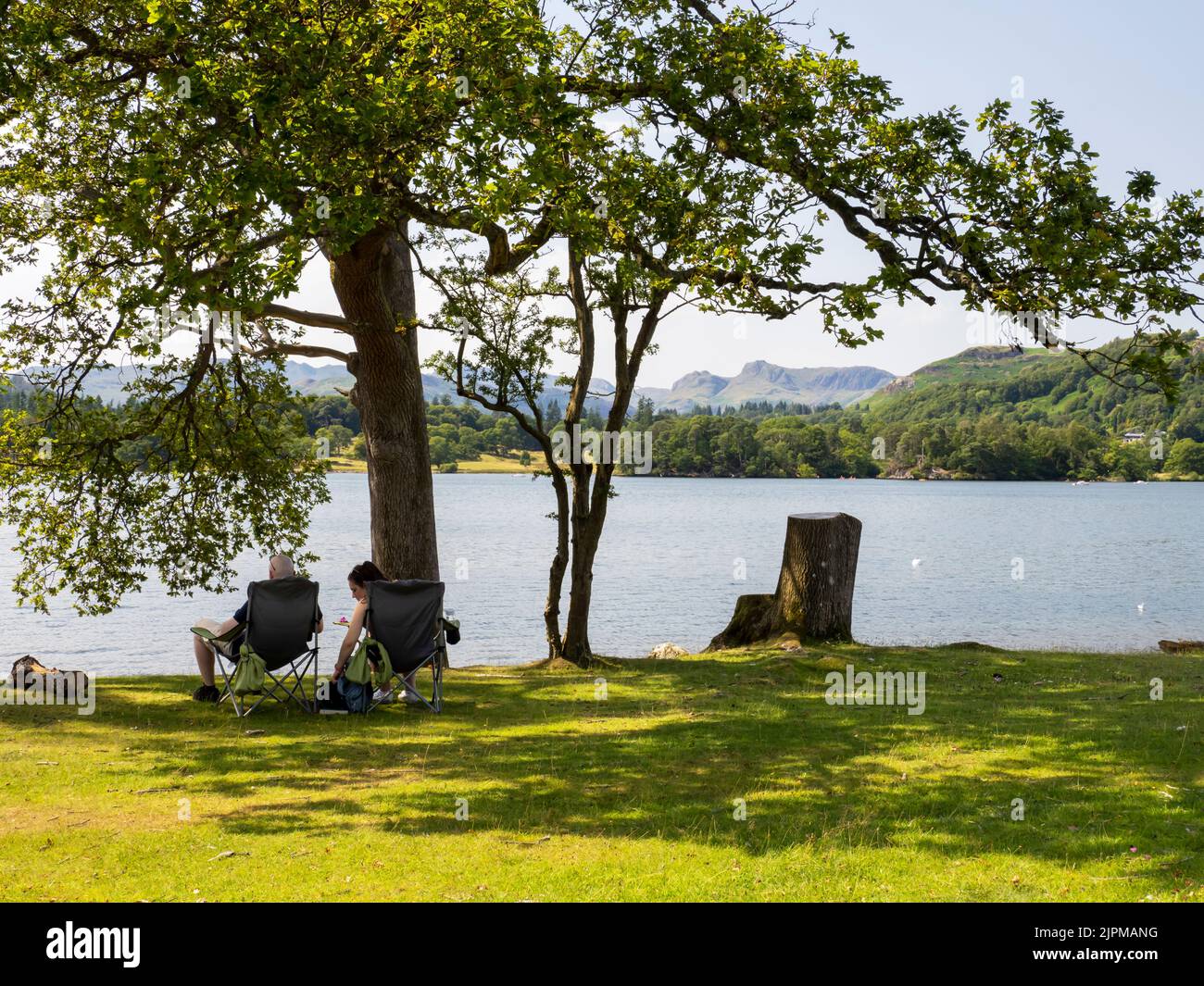 A couple in the shade on the shore off Lake Windermere in the mid July ...