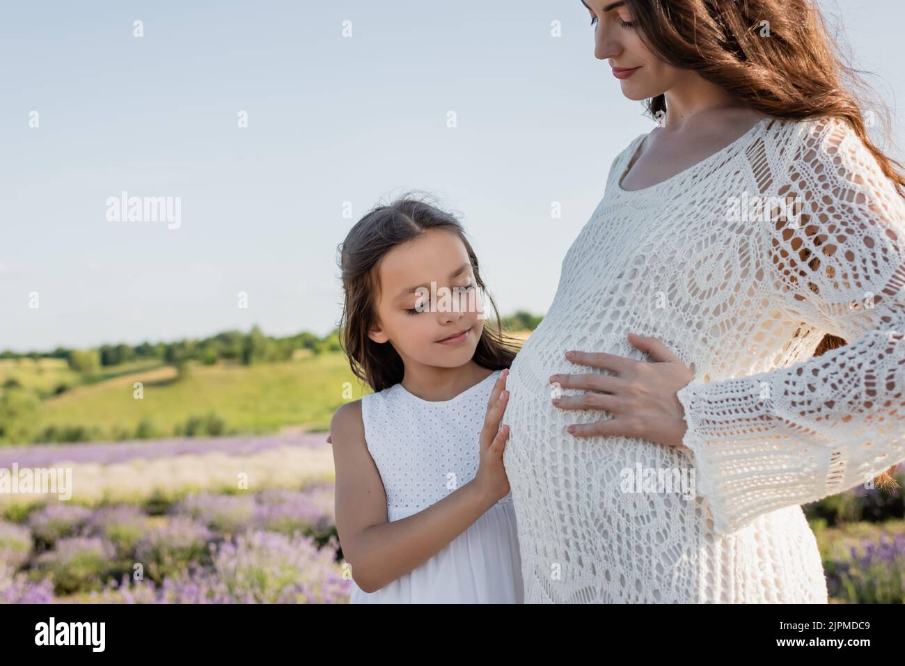 smiling girl hugging tummy of pregnant mother in blurred field Stock ...